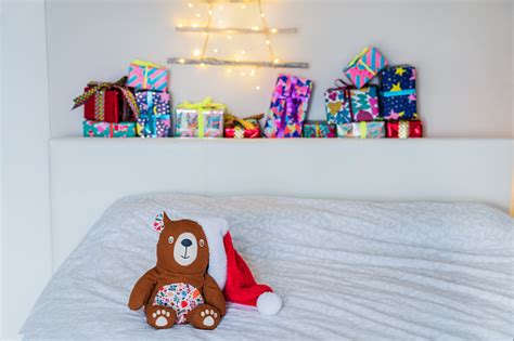 화려한 선물 상자와 벽에 화환 나무 막대기로 만든 크리스마스 트리의 배경에 침대에 산타 모자에 아늑한 장난감 곰 심플하고 미니멀한 인테리어 디자인과 어린이 침실장식 0명에