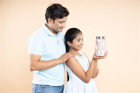 행복한 젊은 인도 아버지와 딸이 베이지색 스튜디오 배경에 고립된 루피 지폐로 가득 찬 유리병을 들고 있다 돈을 절약하고 개념을 투자합니다 2명에 대한 스톡 사진 및 기타