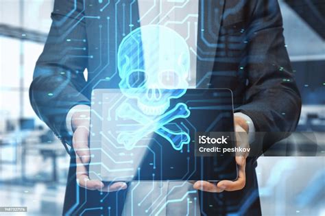 흐릿한 사무실 내부 배경에 빛나는 해골 홀로그램이 있는 태블릿을 들고 있는 남성의 손을 닫습니다 해커 시스템 또는 사이버 공격 개념입니다 이중 노출 가리키기에 대한 스톡