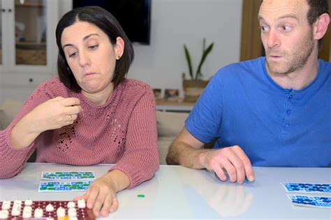 중년의 성인 히스패닉 여성과 빙고 공을 찾는 남자는 이상하고 재미있는 얼굴입니다 가족과 친구들이 즐거운 시간을 보내는 보드 게임