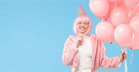 분홍색 모피 코트 모자 가발을 쓰고 파란 배경에 고립된 풍선무리를 들고 왼쪽에 있는 공간을 복사하는 어린 윙크 웃는 생일 소녀의 수평 배너 생일에 대한 스톡 사진 및 기타