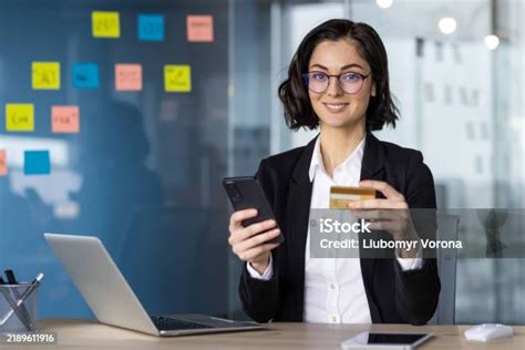 책상 위에 노트북을 올려놓고 현대적인 사무실 환경에서 스마트폰과 신용카드를 사용하는 자신감 넘치는 사업가 Brand Name Smart Phone에 대한 스톡 사진 및 기타