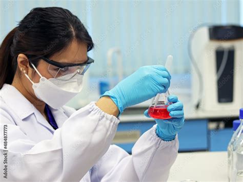 The Scientist Wears Ppe And Holds An Erlenmeyer Flask Laboratory With Red Solvent Solution From