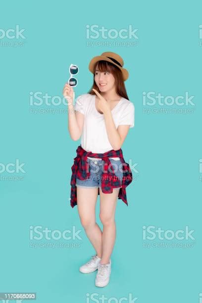 아름 다운 초상화 젊은 아시아 여자 모자를 착용 하 고 선글라스를 들고 자신감 있는 여행 여름 여행 블루 배경에 고립 된 여행 여름 여행을 즐길 수 여행 으로 가리키는 관광