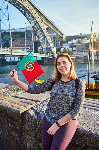 포르투갈어 국기와 함께 다시 서 있는 젊은 여성 여행자 포르투 포르투갈에서 아침에 빛을 하는 동안 도우로 강 다리와 보트에서 아름 다운 도시 경관 감상 건물 외관에 대한