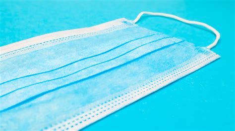 파란색 배경에 입과 코를 덮고 고무 그립이있는 3 Ply 일회용 수술 용 얼굴 마스크 박테리아 의료 및 의학 개념으로부터 보호