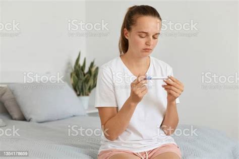 임신 검사를 손에 들고 캐주얼 한 옷을 입고 거실소파에 앉아 긍정적 인 결과를 얻기 위해 화가 원치 않는 임신을 가진 슬픈 여자의 실내 샷 여자에 대한 스톡 사진 및 기타