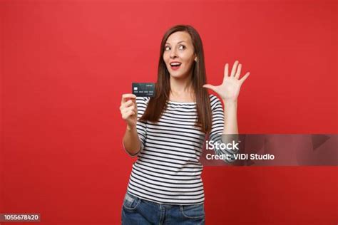 줄무늬 옷 찾고 신용 카드를 들고 밝은 빨간 벽 배경에 고립 된 팜 보여주는 호기심 젊은 여자의 초상화 사람들이 진심으 감정 라이프 스타일 개념 복사 공간을 비웃는 다 갈색