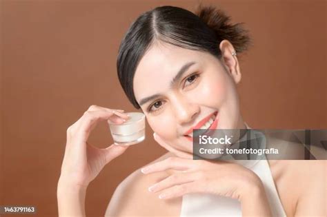 아름다운 얼굴을 가진 젊은 여자는 그녀의 얼굴의 크림을 사용하여 크림을 들고 있습니다 아름다움 피부 관리 개념 갈색 배경에 대한 스톡 사진 및 기타 이미지 Istock