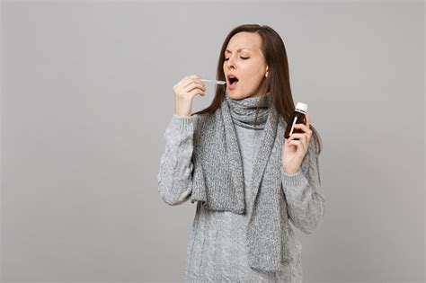 회색 스웨터에 아픈 젊은 여자 스카프는 회색 벽 배경에 고립 된 숟가락에 액체 약을 붓는 다 건강 한 라이프 스타일 아픈 질병