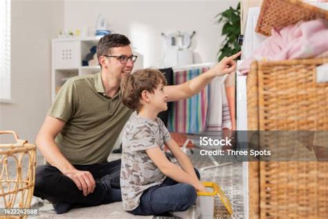 아버지는 세탁실 욕실에서 어린 아이들과 시간을 보내고 출산 휴가 기간 동안 가사 의무를 수행하고 아들을 돌보고 소년에게 세탁기 작동 방법을 보여줍니다 2명에 대한 스톡 사진