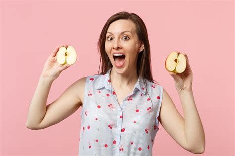 여름 옷에 흥분 된 젊은 여성이 분홍색 파스텔 배경에 고립 된 신선한 잘 익은 사과 과일의 Halfs를 유지 입을 열어 사람들은 생생한 라이프 스타일 휴식 휴가 개념입니다