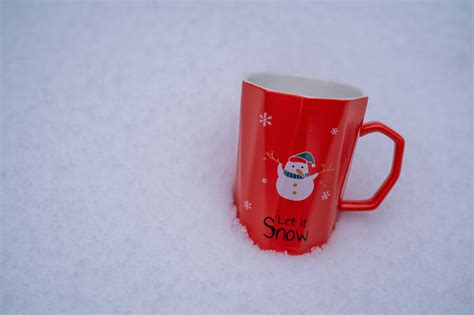 눈사람이 프린트 된 빨간 머그잔과 눈 텍스트를 보자 뜨거운 음료 컵은 하얀 눈 위에 서 있습니다 겨울 크리스마스 휴일과 새해 전야 축하 냉각 효과 예열 12월에 대한 스톡