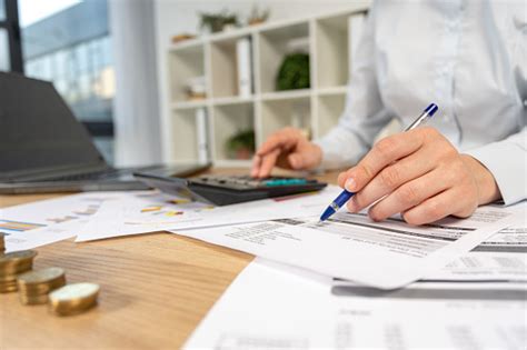 자른 그녀 차트 로프트 인테리어 직장 확인 청구서에 그래프 그래픽에 쓰기 빈 펜 초점에 의해 반면에 데스크톱 테이블 뒤에 앉아 그녀의 Formalwear 셔츠에 집중된