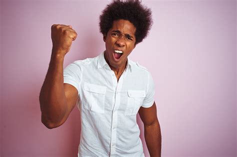 고립 된 분홍색 배경 에 서 흰색 셔츠를 입고 아프리카 머리를 가진 젊은 미국 남자는 분노와 함께 외치는 동안 좌절과 분노를