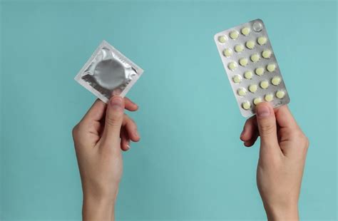 As mãos seguram preservativos na embalagem pílulas anticoncepcionais
