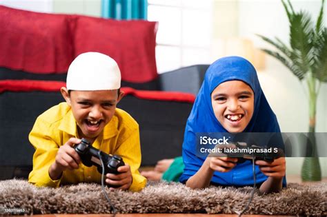 집에서 바닥에 누워있는 동안 조이스틱을 사용하여 비디오 게임을하는 두 무슬림 형제 아이들 아이들의 개념 건강에 해로운 재생 위치와 게임 중독 다양성에 대한 스톡 사진 및