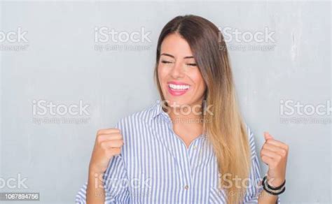 그런 지 위에 젊은 성인 여자 회색 벽 매우 행복 하 고 흥분 무기와 우승자 제스처를 하 고 비즈니스 셔츠를 입고 웃 고 성공을