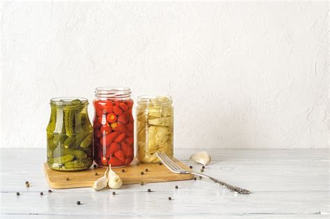 흰색 나무 테이블에 통조림 야채가있는 유리 항아리를 엽니 다 기름에 아티초크 절인 거킨과 작은 붉은 고추를 먹을 준비가 되어 있습니다 발효 유기농 야채 간식과 조미료 0명에