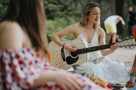 Young Girls Enjoying A Picnic While Playing Guitar Outdoors In Nature