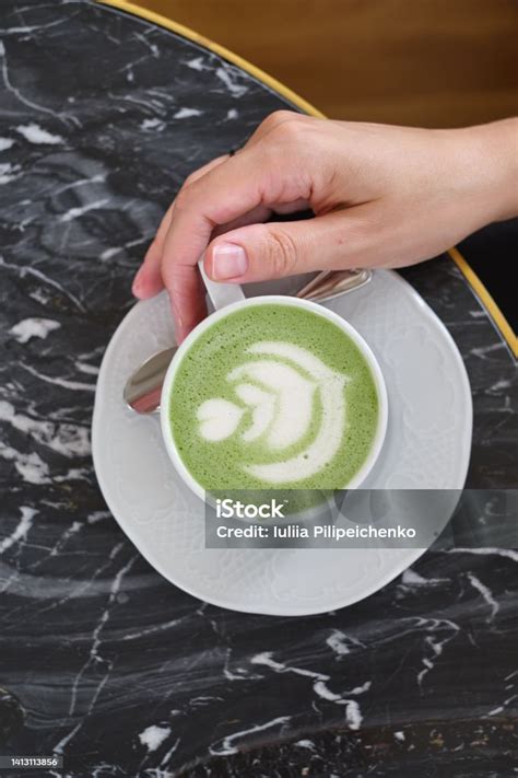 말차 라떼 한 잔을 든 여성이 카페에 앉아 있습니다 녹색 컵 클로즈업에 맛있는 녹차 차 일본의 뜨거운 우유 음료 유기농 재료로 만든 건강한 말차 가루로 빻은에 대한 스톡