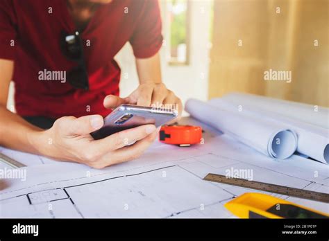Engineer Or Architect Using Cell Phone On Blueprint In Building Construction Site Stock Photo
