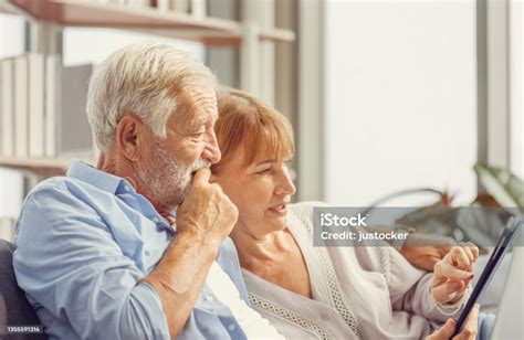 거실에서 행복한 시니어 부부의 초상화 노인과 집에서 아늑한 소파에 태블릿 스마트 폰을 사용하는 여자 행복한 가족 개념 여자 노인에 대한 스톡 사진 및 기타 이미지 Istock