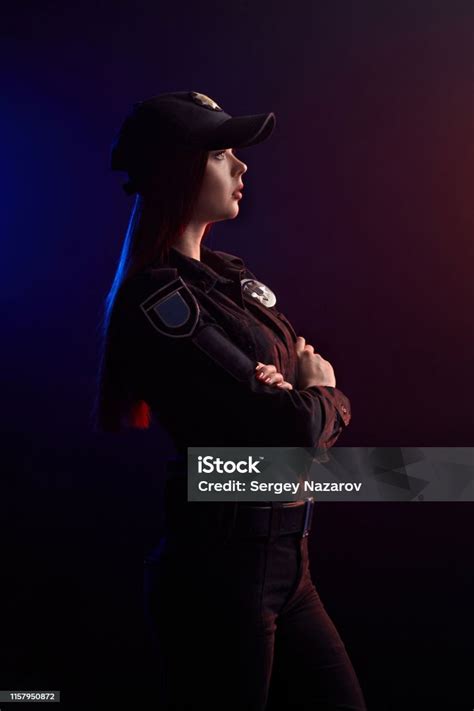 심각한 여성 경찰관은 빨간색과 파란색 백라이트와 검은 배경에 대한 카메라를 위해 포즈를 취하고있다 검은색에 대한 스톡 사진 및