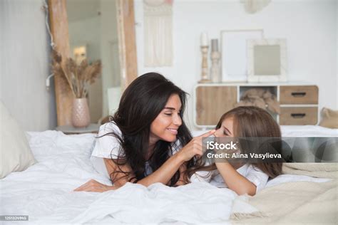 행복한 사랑하는 가족은 함께 침실에서 휴식을 취하고 즐기고 있습니다 어머니와 그녀의 귀여운 유치원 딸 소녀 잠옷에 놀고 아침에 흰색 침대에서 껴안고 행복한 어머니의 날 2