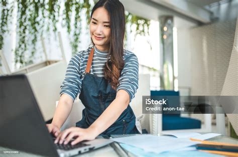 젊은 아시아 여성 바리스타가 도시 카페에서 행복한 미소를 짓고 있는 모습 앞치마에 있는 중소기업 오너 한국 소녀는 테이블에 앉아 노트북 컴퓨터에 메모를 하는 여성을 긴장시다