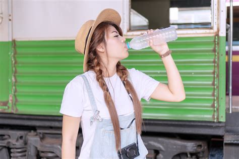 여행자 젊은 여성은 기차역에서 누군가를 기다리는 동안 그녀의 손에 신선한 물 양식 병을 마시는 카메라와 모자를 착용 라이프 스타일 여행 휴식 개념 20 24세에 대한 스톡