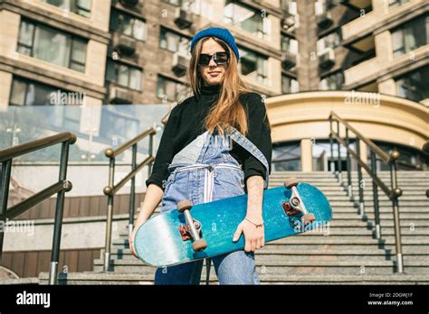 Stylishly Dressed Woman In Blue Denim Jumpsuit Posing With Skateboard