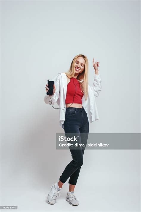 좋아하는 노래 아름 다운 젊은 여자의 전체 길이 초상화 그녀의 스마트 폰으로 음악을 듣고 춤과 웃는 회색 배경에 서 있는 동안 귀여운에 대한 스톡 사진 및 기타 이미지