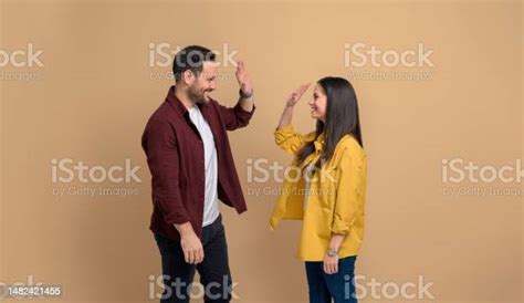 셔츠를 입고 웃고 있는 젊은 부부가 서로에게 하이파이브를 하고 승리를 축하한다 쾌활한 남자와 여자는 외딴 베이지색 배경에 서서 손뼉을 치고 인사한다 하이 파이브에 대한 스톡