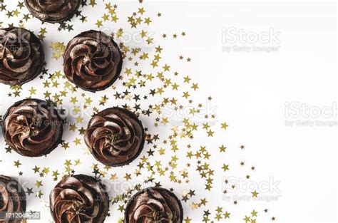 초콜릿 아이싱과 황금 별 모양의 색종이와 흰색 배경에 금 빛을 뿌린 초콜릿 컵 케이크 휴일 개념입니다 디자인에 대한 모형 플랫 레이 스타일입니다 공간을 복사합니다 0명에