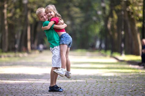 두 귀여운 재미 웃는 웃는 아이들 소녀와 소년 그의 팔에 여동생을 들고 형제 흐릿한 밝은 햇볕이 잘 드는 공원 골목 녹색 나무 보케 배경에 재미를 사랑 형제 관계 개념