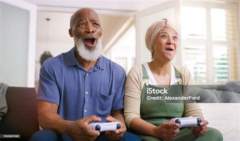 노부부는 거실에서 함께 비디오 게임을 하며 현대적인 집에서 도전을 한다 행복하고 경쟁적이며 흥분된 노인 남녀 게이머가 집에서 소파에서 은퇴 게임을 하고 있습니다 노인 남자에