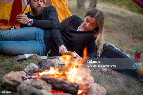 아름 다운 커플 앉아 캠프 파이어 주위에 캠핑 텐트와 배경에 남자 막대기로 화재 제스처 건강한 생활방식에 대한 스톡 사진 및 기타 이미지 Istock