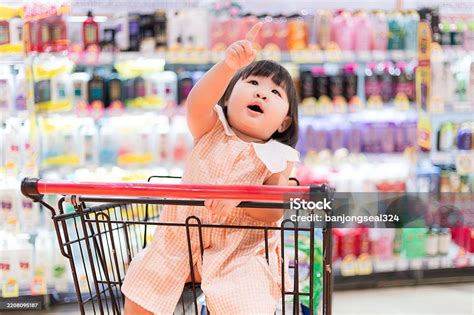 아시아 유아는 쇼핑몰의 쇼핑 카트에 앉아 있으며 12 세 아기의 초상화 이미지 슈퍼마켓에서 쇼핑하는 카트에 앉아 있는 행복한 아시아 어린이 소녀 18 23 개월에 대한 스톡