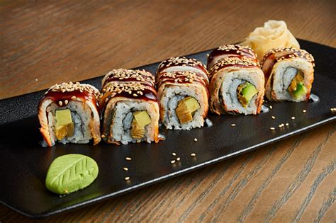 식욕을 돋우는 스시 롤 황금 용 장어 데리야키 소스 아보카도를 나무 배경에 검은 접시에 얹은 롤 포스트 중 필름 효과 소프트 포커스 열 개념에 대한 스톡 사진 및 기타