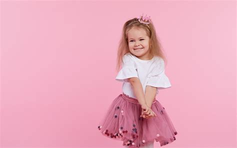 분홍색 배경에 고립 된 그녀의 머리에 얇은 명주 그물 스커트와 공주 왕관을 가진 쾌활한 어린 소녀 아이들을위한 활기찬 카니발을 축하 생일 파티 재미 공주에 대한 스톡 사진