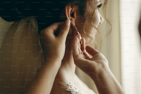 하얀 웨딩 드레스에 갈색 머리 신부를 돕는 아름다운 신부 들러리는 고급 귀걸이 아침 결혼식 준비 귀걸이 클로즈업을 가진 신부 사진 Unsplash의 남편과 아내 이미지