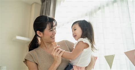 아시아의 아름다운 사랑하는 어머니는 어린 여자 딸을 팔에 안고 빙글빙글 돌고 있습니다 매력적인 부모는 어린 작은 소녀와 미소 놀이로 서 있습니다 가정에서의 육아 활동