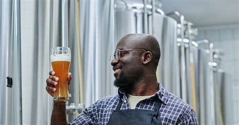 아프리카계 미국인 엔지니어가 맥주 한 잔을 들고 미소를 지으며 음료의 질에 만족했습니다 사진 Unsplash의 공장 이미지