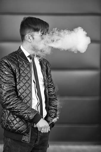 Vape 남자입니다 비행 선글라스 Vaping에 전자 담배에서 증기 시키는 현대이 발과 잘생긴 젊은 백인 남자의 초상화 흑인과 백인 사진입니다 거리에 대한 스톡 사진 및