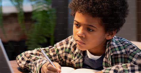 노트북 앞 테이블에 앉아 온라인 수업 중 디스플레이를 보면서 카피북에 메모를 하는 진지한 아프리카 남학생 사진 Unsplash의 아프리카 계 미국인 민족 이미지