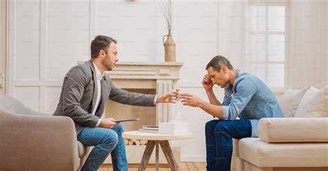 슬픈 순간 소파에 앉아 아래를 내려다 보는 불안정한 남성 환자에게 물 한 잔을주는 숙련 된 심리학자 사진 Unsplash의 정신 건강 이미지