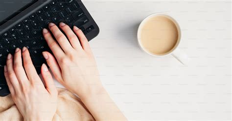 노트북 키보드 평면도에 텍스트를 입력하는 여성 손 담요 커피 컵 노트북이 있는 현대적인 미니멀한 여성 작업 공간 사진