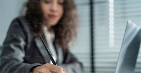 사무실에서 일하는 동안 라틴계의 아름다운 비즈니스 우먼의 미소를 닫습니다 정장을 입은 매력적인 전문 여성 직원이 직장에서 테이블에 앉아 노트북 컴퓨터를 사용하고 책에