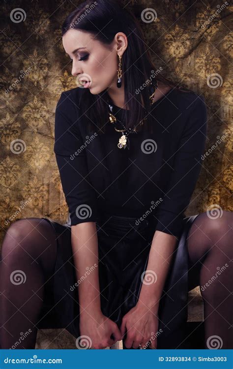 Sensual Fashion Model In Black Clothes With Jewellery Over Golden Pattern Background Stock Photo